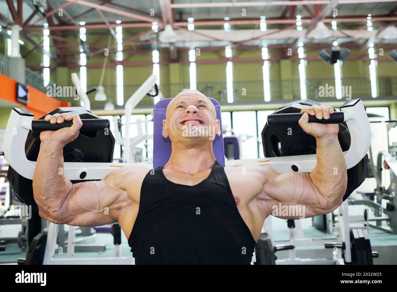 Bodybuilder in black jersey trains on exercise machine in gym hall ...