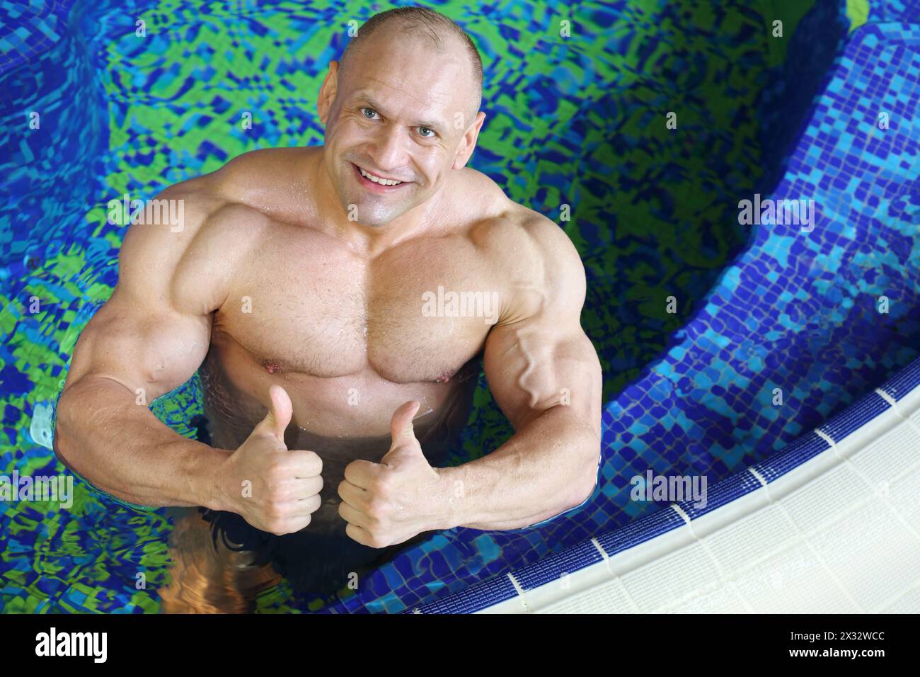 Top view of happy bodybuilder showing thumbs-up gesture in swimming ...