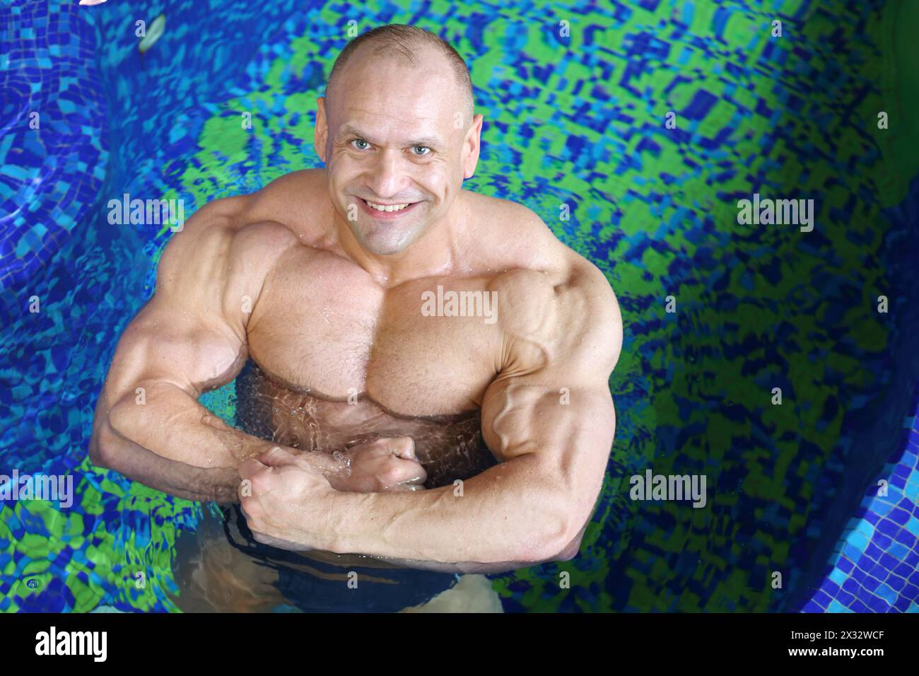 Top view of happy middle-aged bodybuilder standing in swimming pool ...