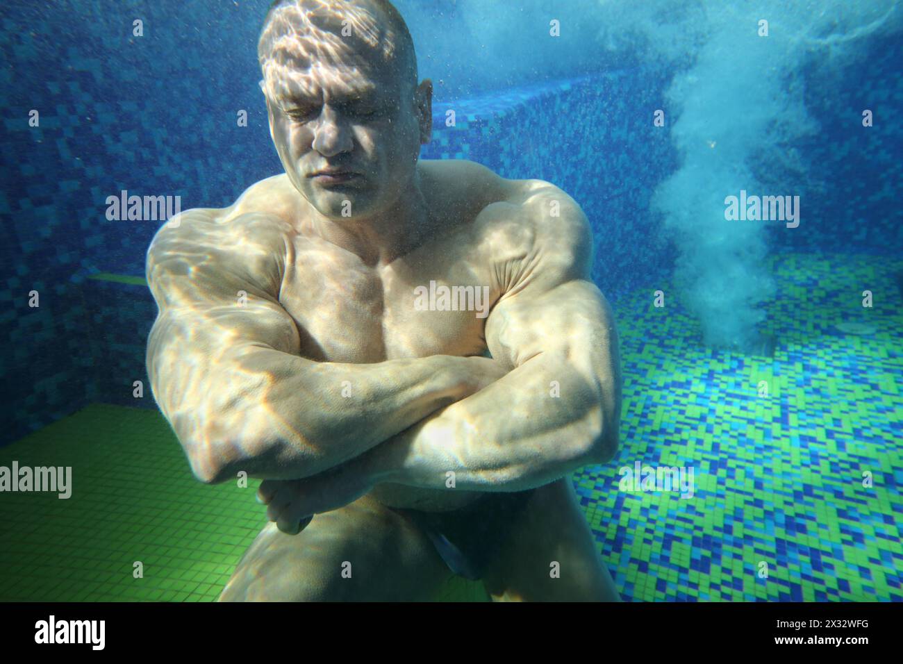 Bodybuilder with closed eyes on bottom of pool underwater among small ...