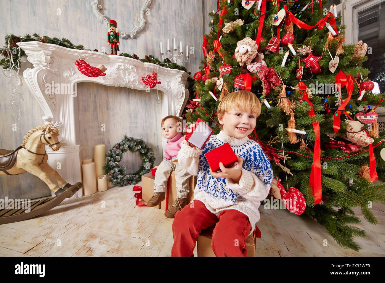 Little boy and little girl sit on big gift boxes under Christmas tree ...