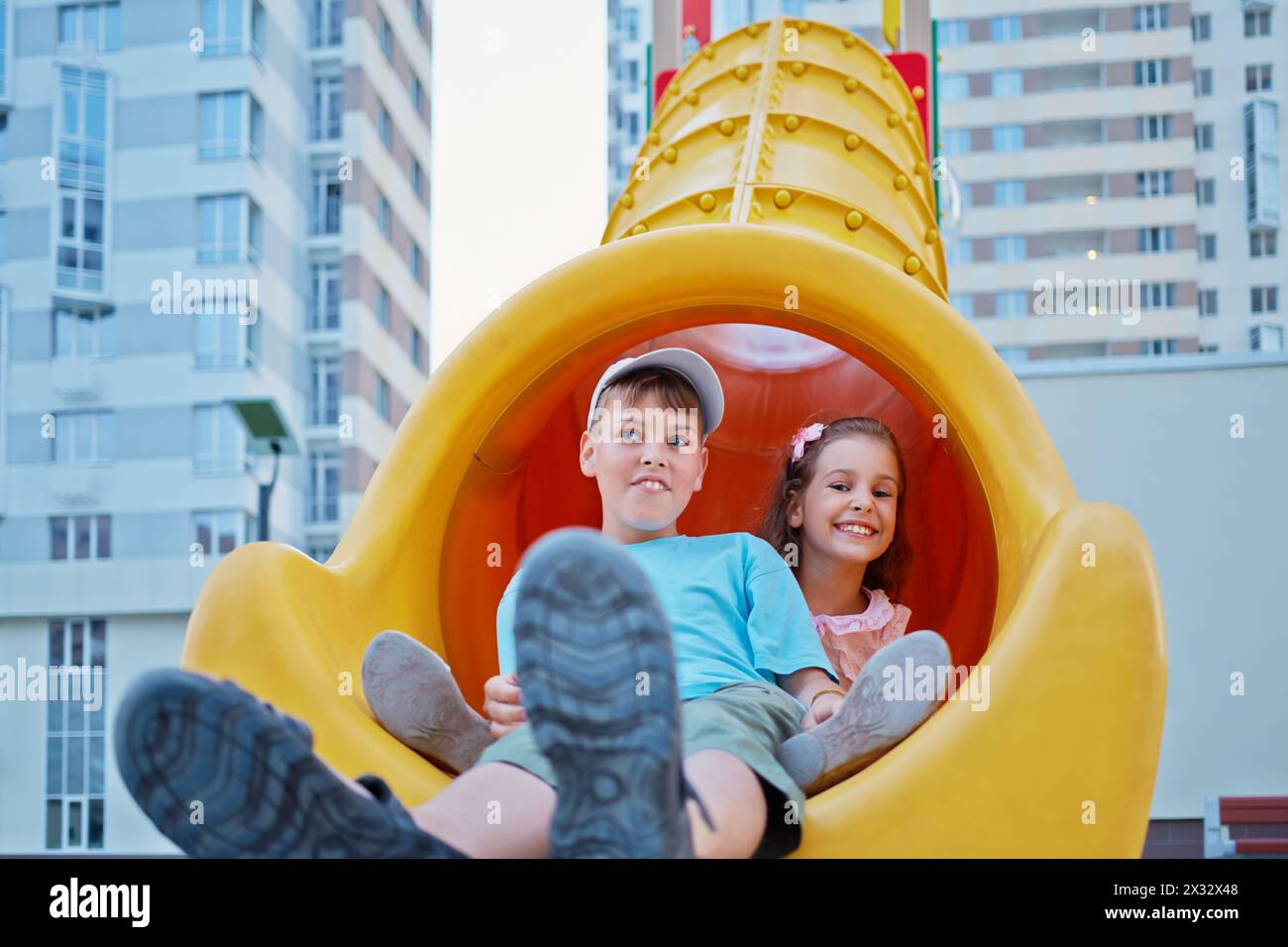 Boy and his younger sister sit at bottom of slide on children ...