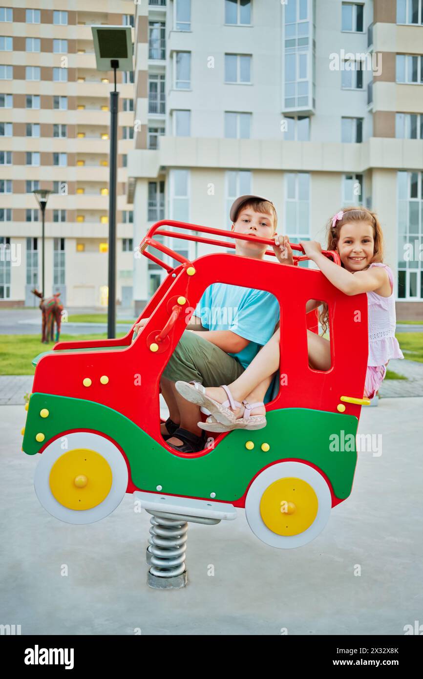 Boy and girl ride on spring swing at children playground in house yard ...