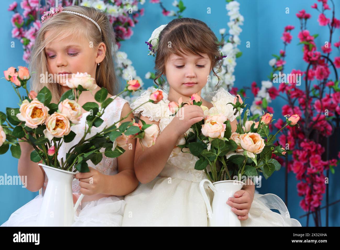 Two little girls in white dresses looks at bouquets of roses in room ...