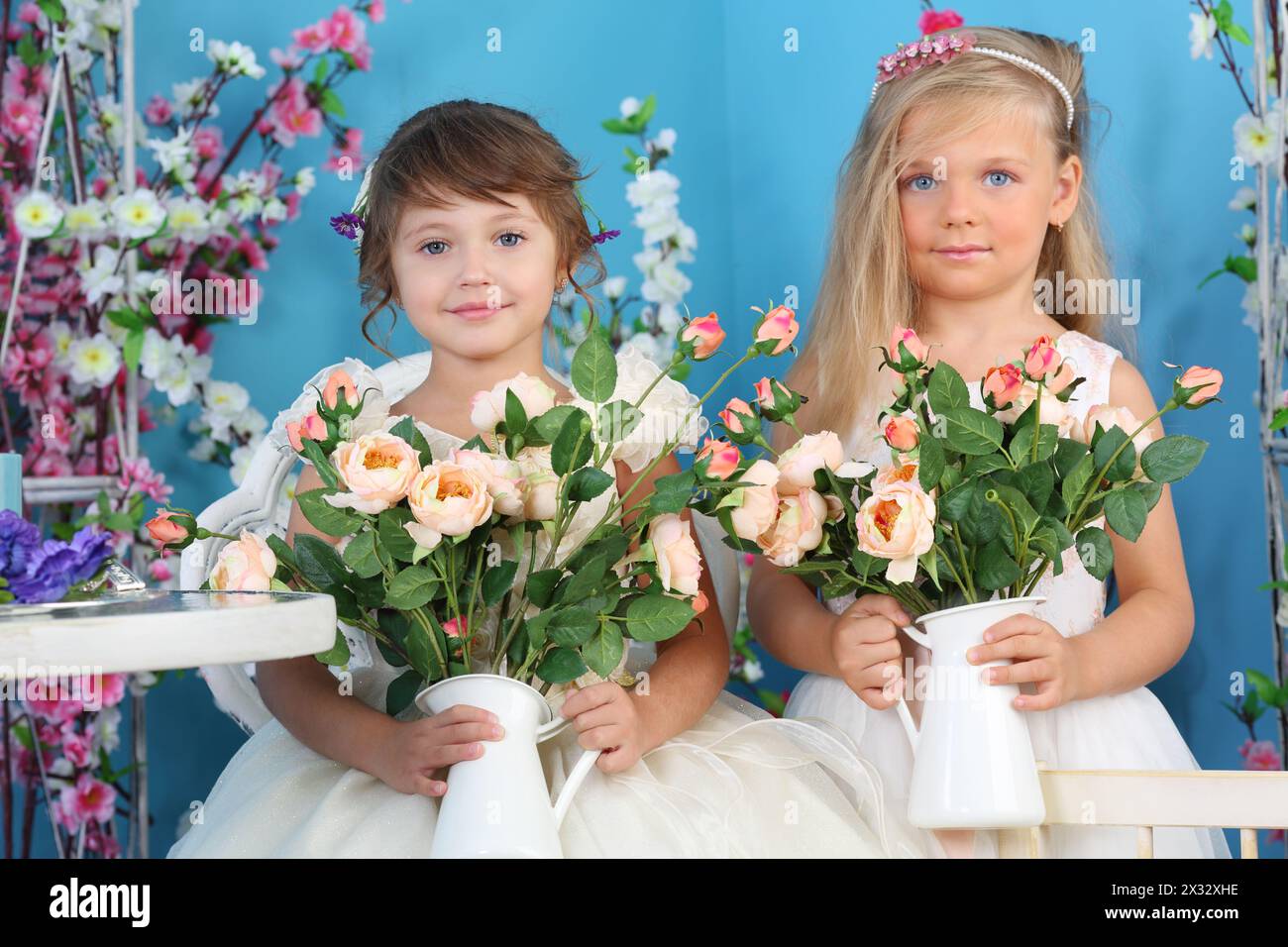 Two pretty little girls in white dresses hold roses in room with ...