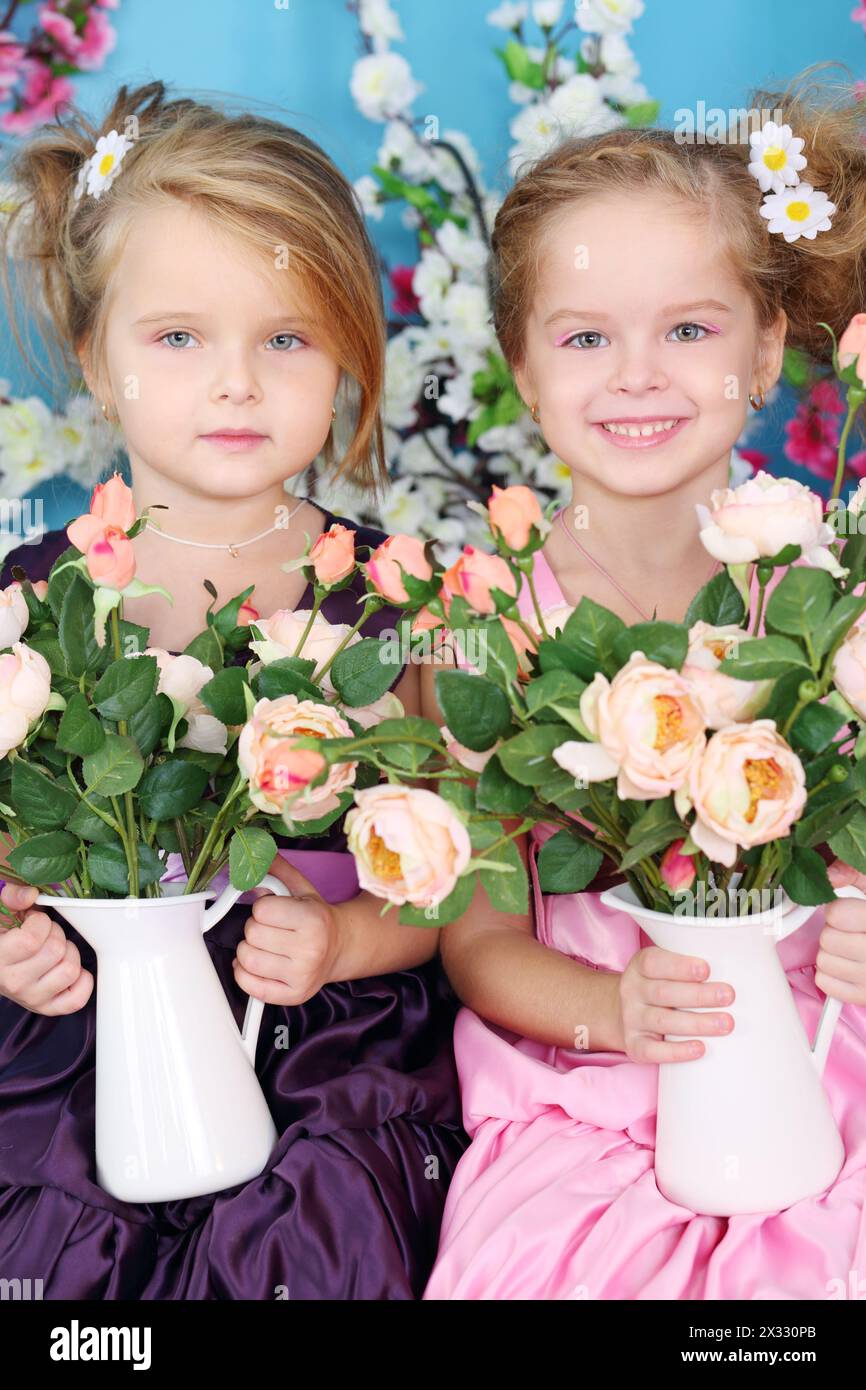 Two little girls in dresses hold bouquets of roses in pitchers and ...