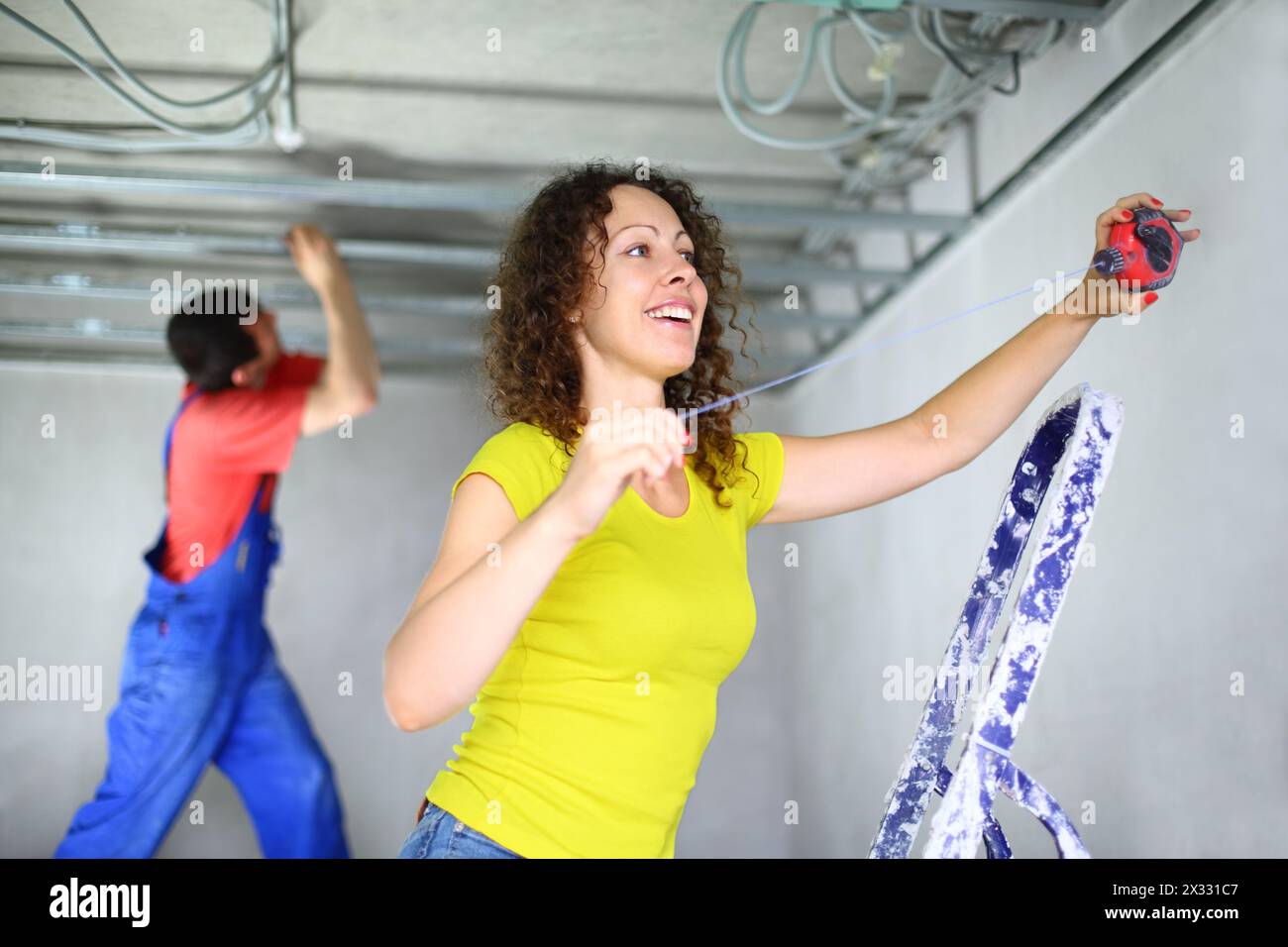 A young woman is standing on a ladder with an edge line marker, man is ...