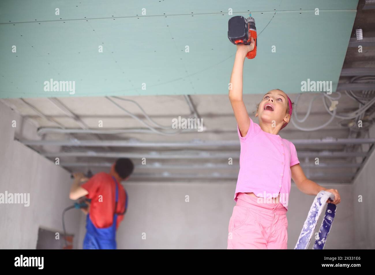 The girl with an electric screwdriver to fasten drywall on ceiling and ...