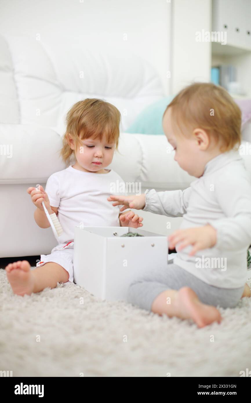 Two little girls sit on carpet and play with white box. Focus on left ...