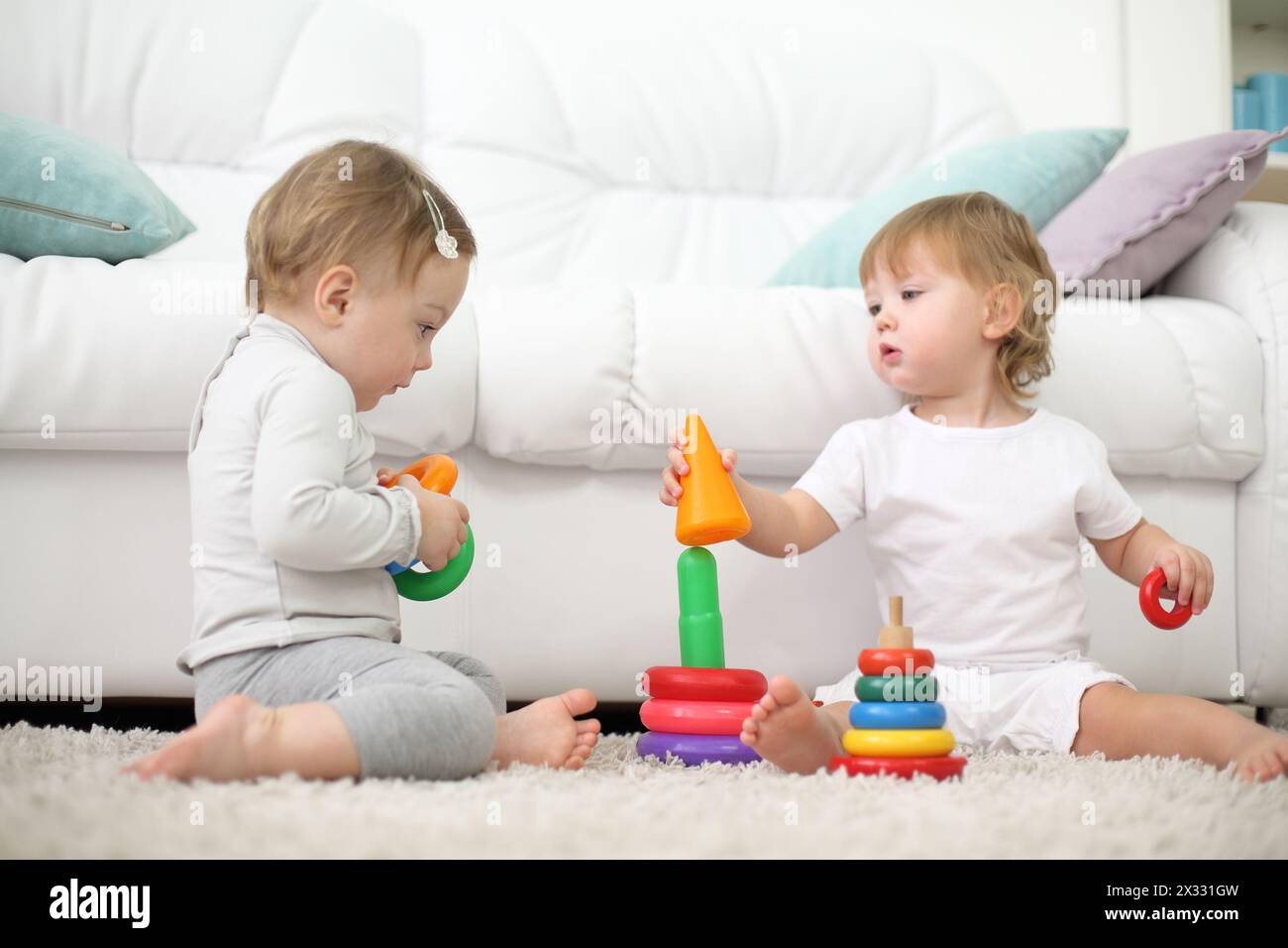 Two barefoot kids sit on carpet and play with pyramids near sofa. Focus ...