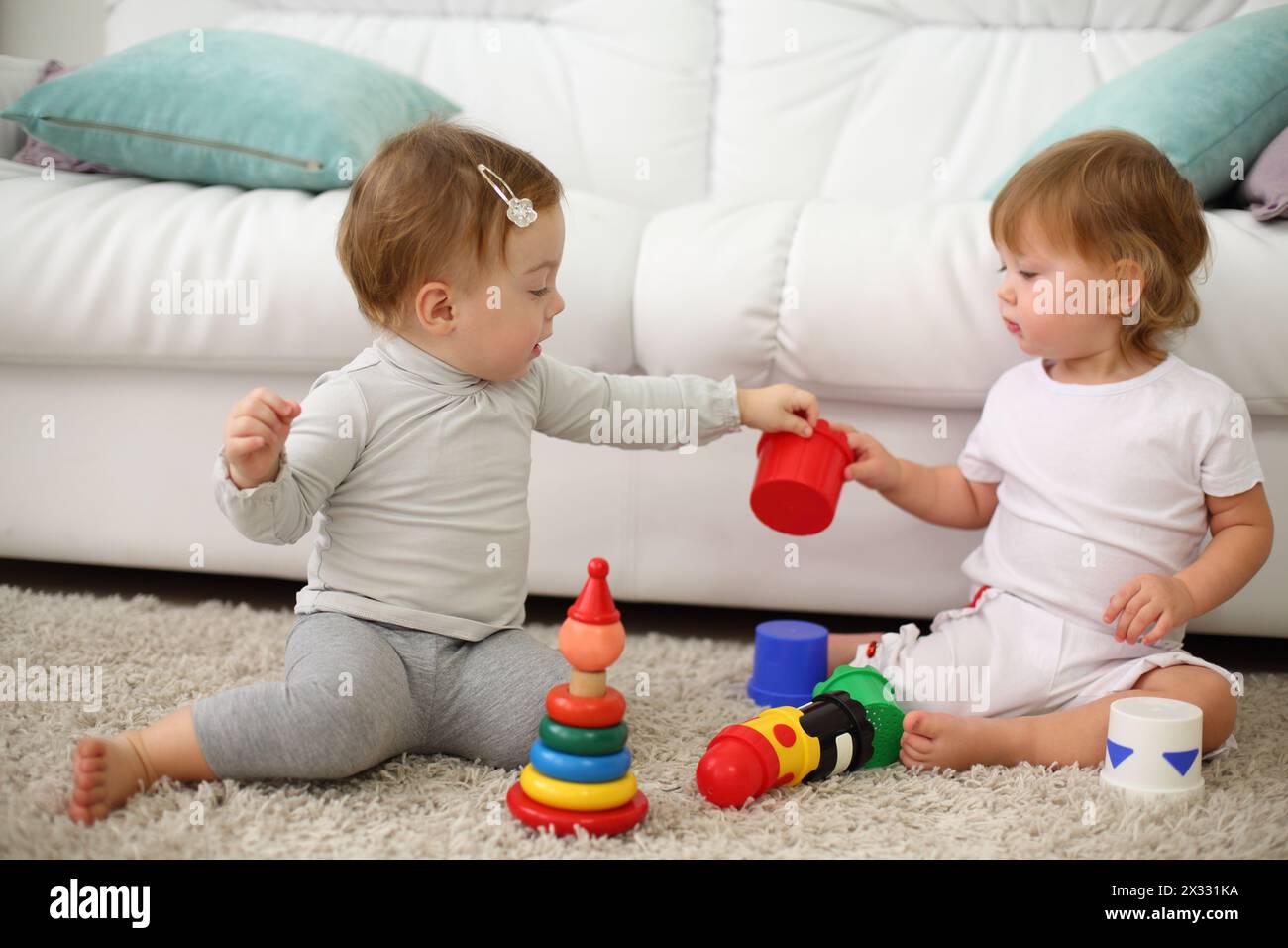 Two barefoot kids sit on carpet and play with colored toys near sofa ...