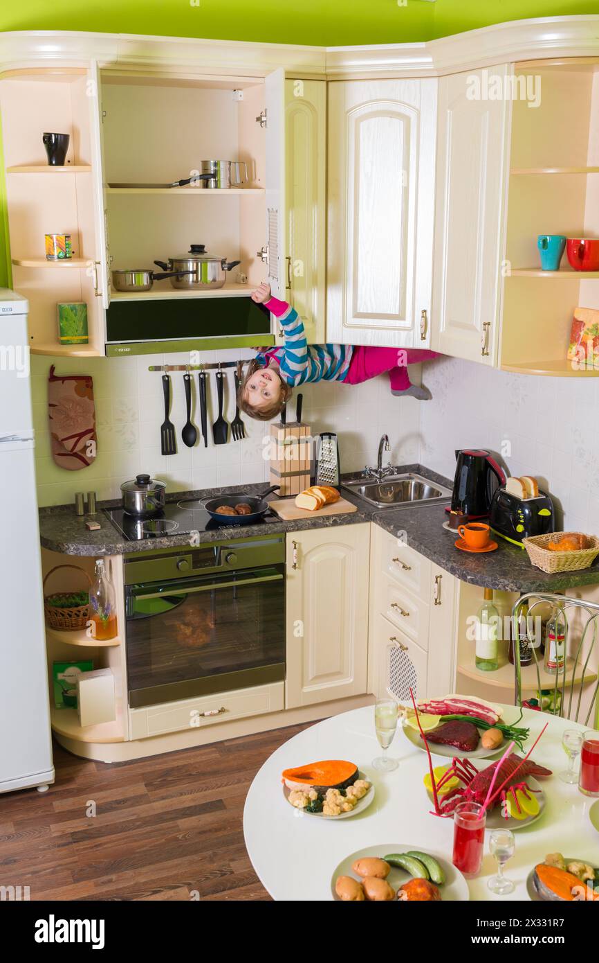 Little girl upside down holds a shelves in the kitchen with table and ...