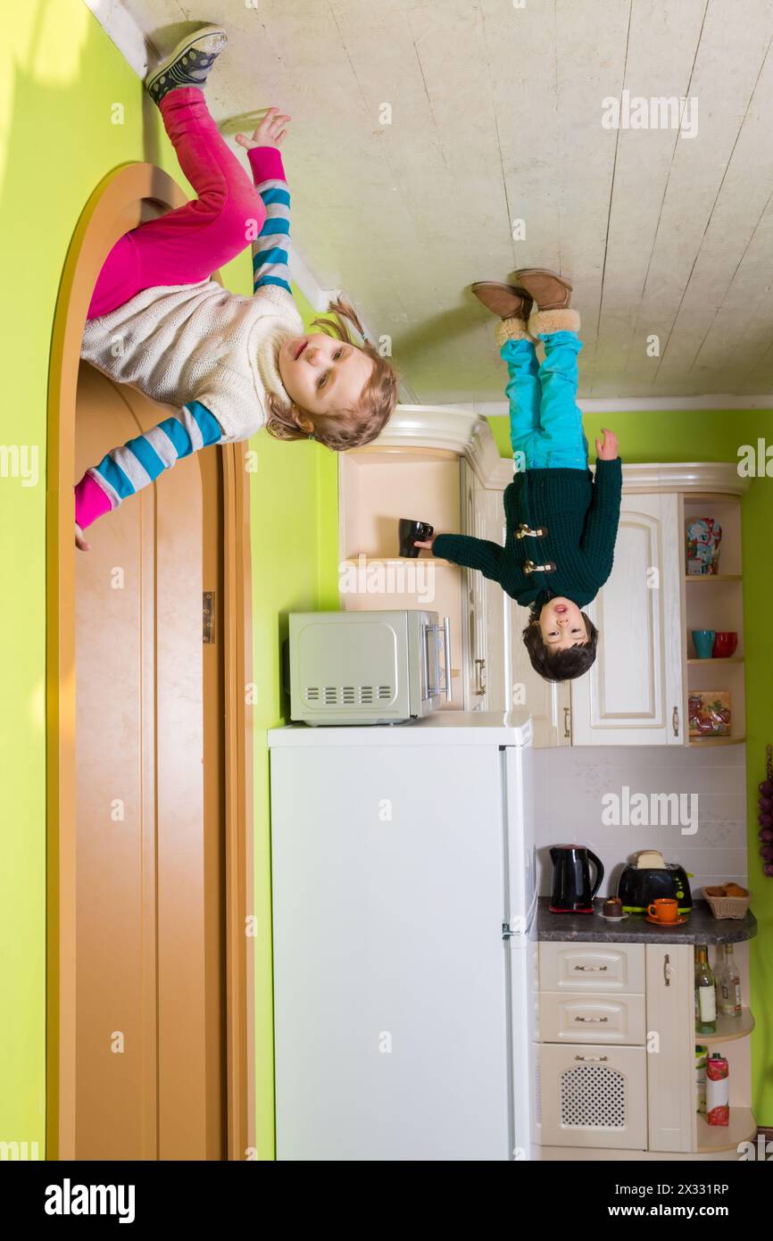 Two children upside down on the ceiling of kitchen at inverted house ...