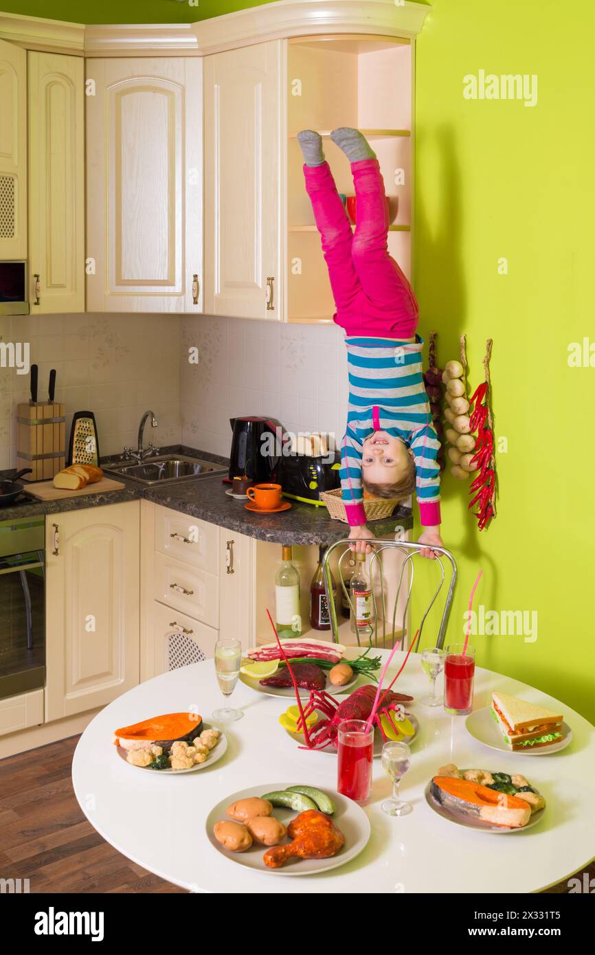 Little girl upside down holds a chair in the kitchen with table and ...