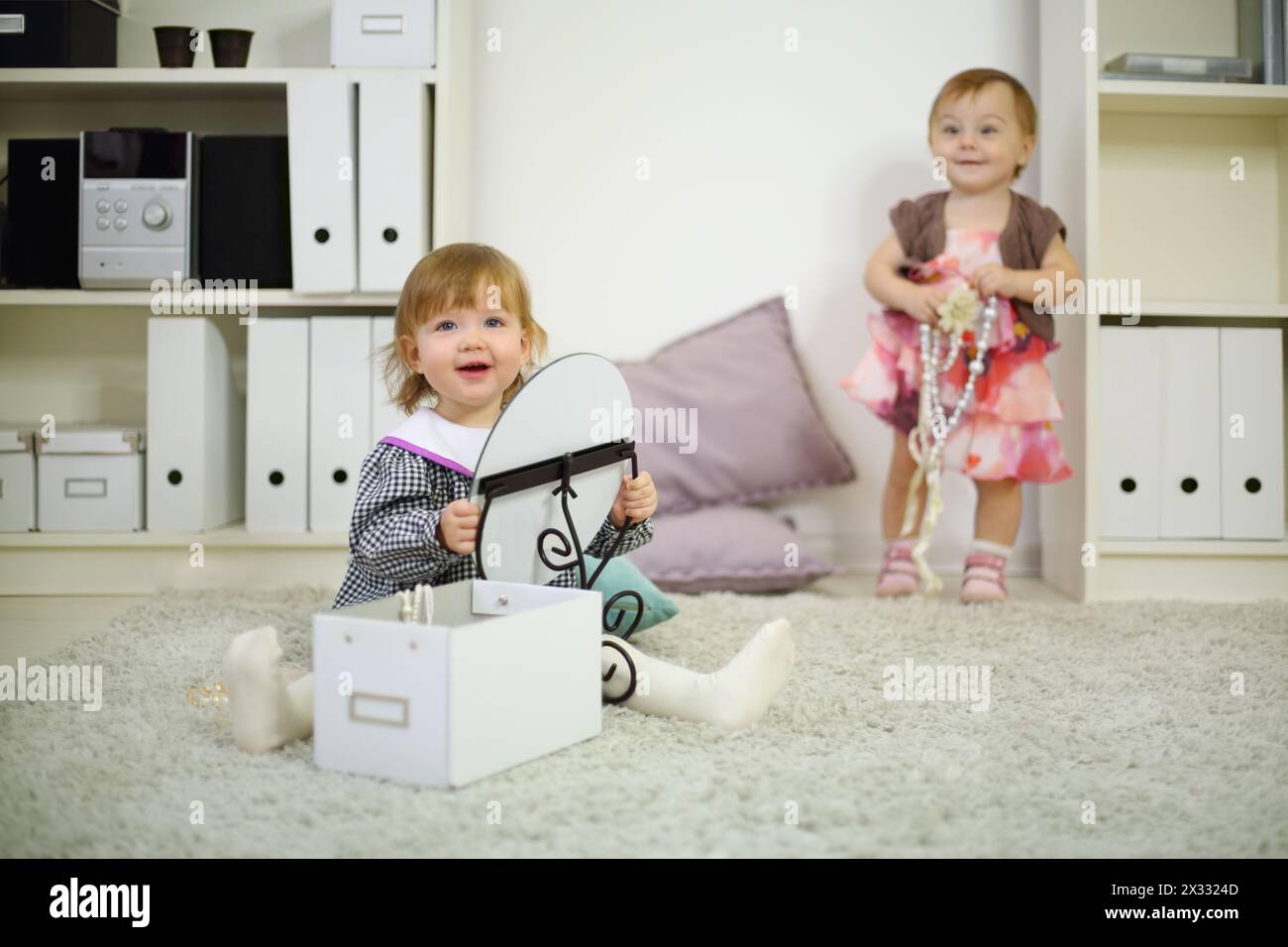 Two happy little girls play on white carpet with mirror and beads at ...
