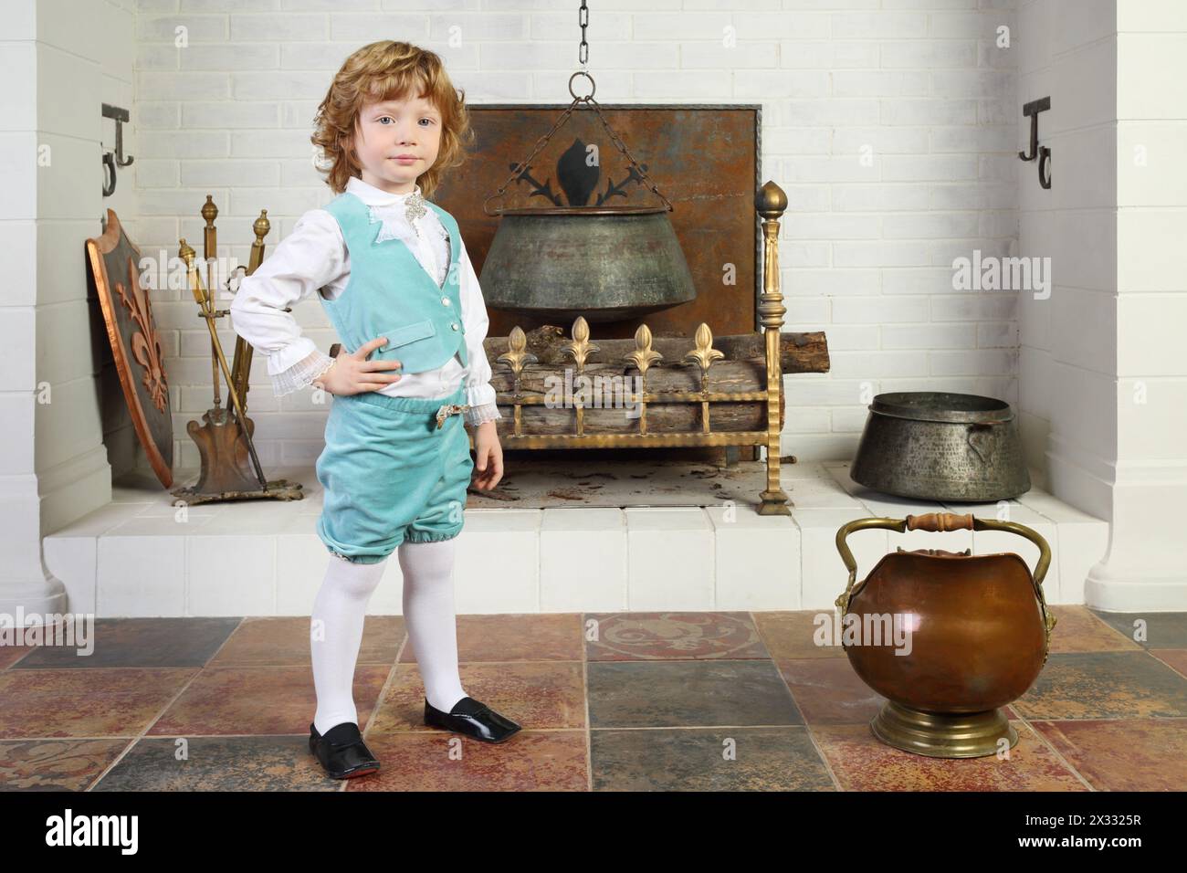 Little boy in medieval costume stands near fireplace with logs and ...