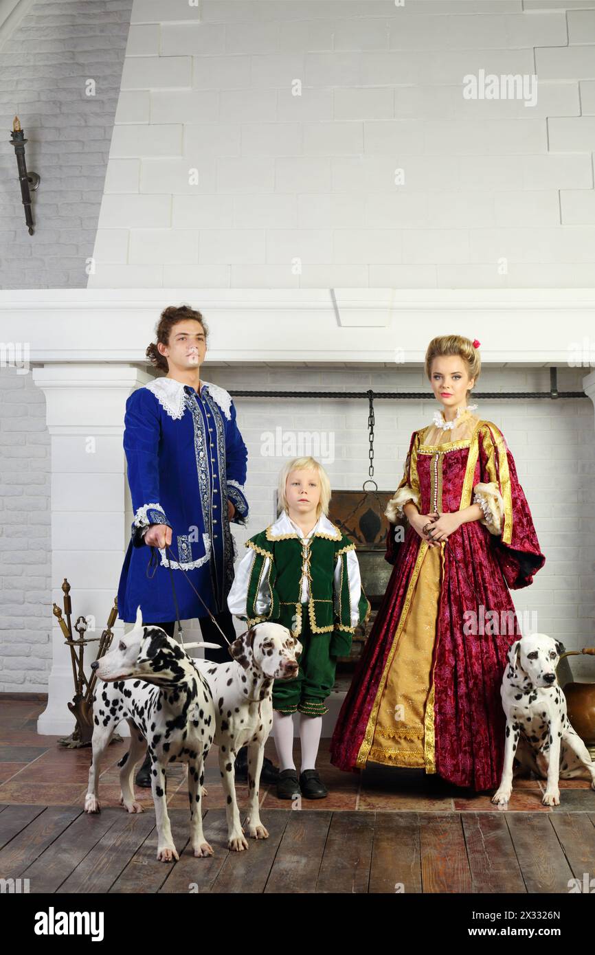 Father, mother and son in bright medieval costume stand near fireplace ...