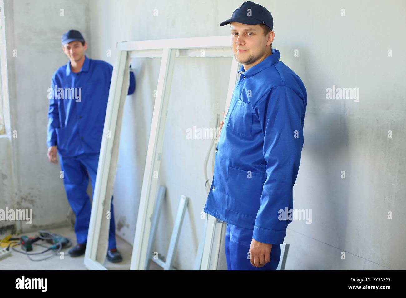Two men in work clothes with the new window frame in a room under ...