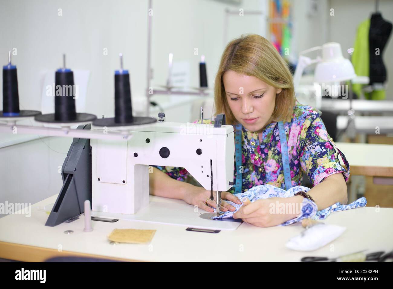 Pretty female tailor sits at table with sewing machine and sews fabric ...