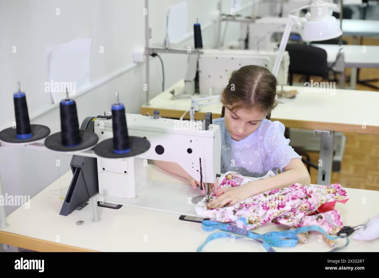 Student girl sews small dress at white sewing machine in classroom with ...