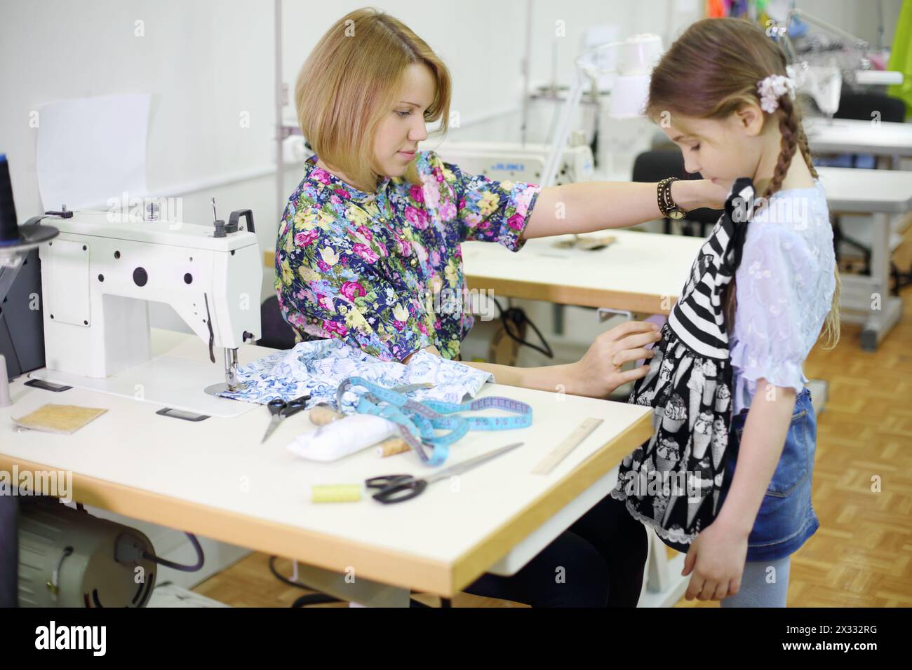 Female tailor sits at table with sewing machine and applies dress to ...