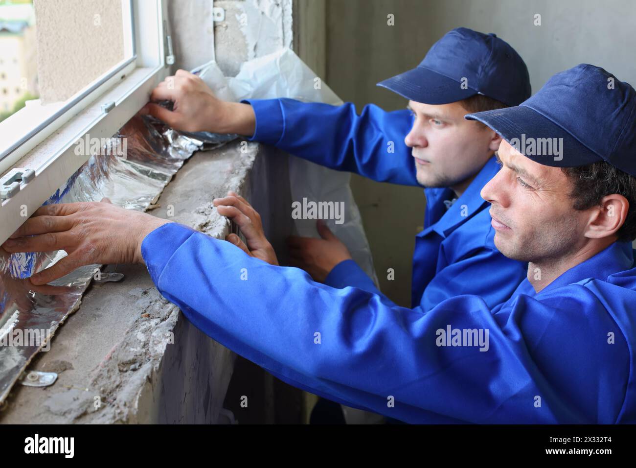 Two men in working clothes places the foiled insulation on the window ...