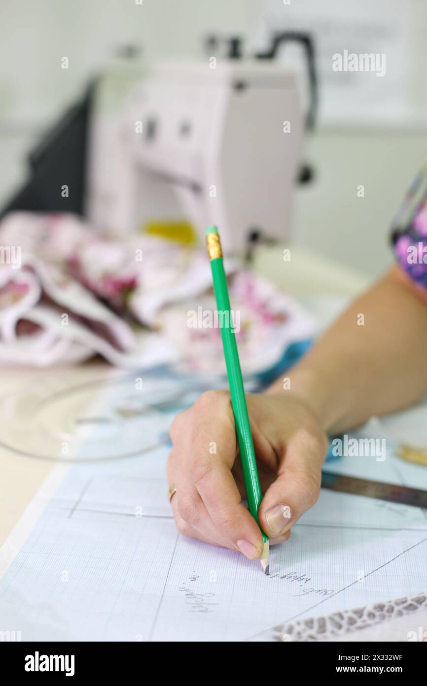 Hand of female tailor drawing pattern at paper near white sewing ...