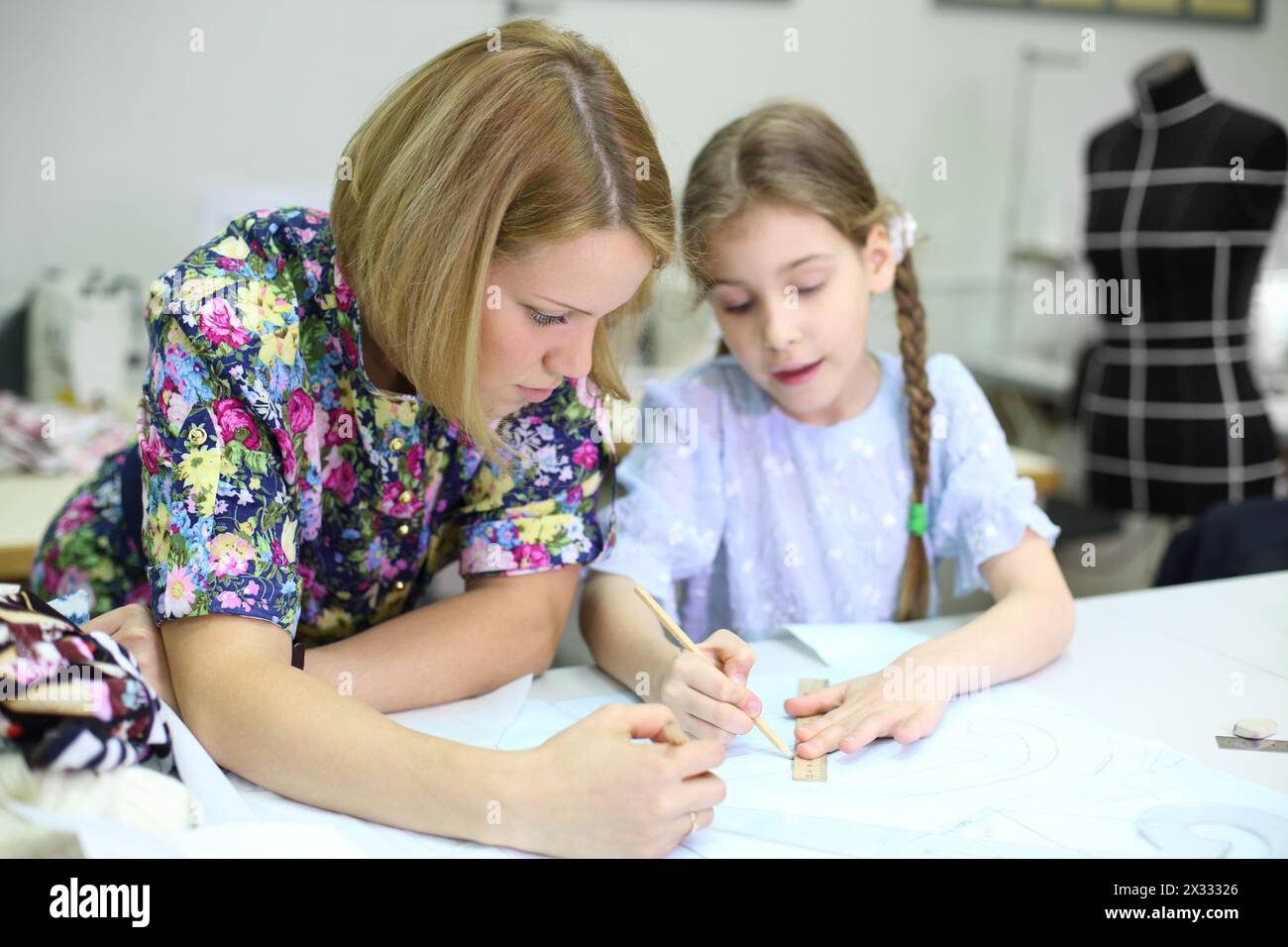 Female tailor looks how student girl draws patterns for clothes. Focus ...