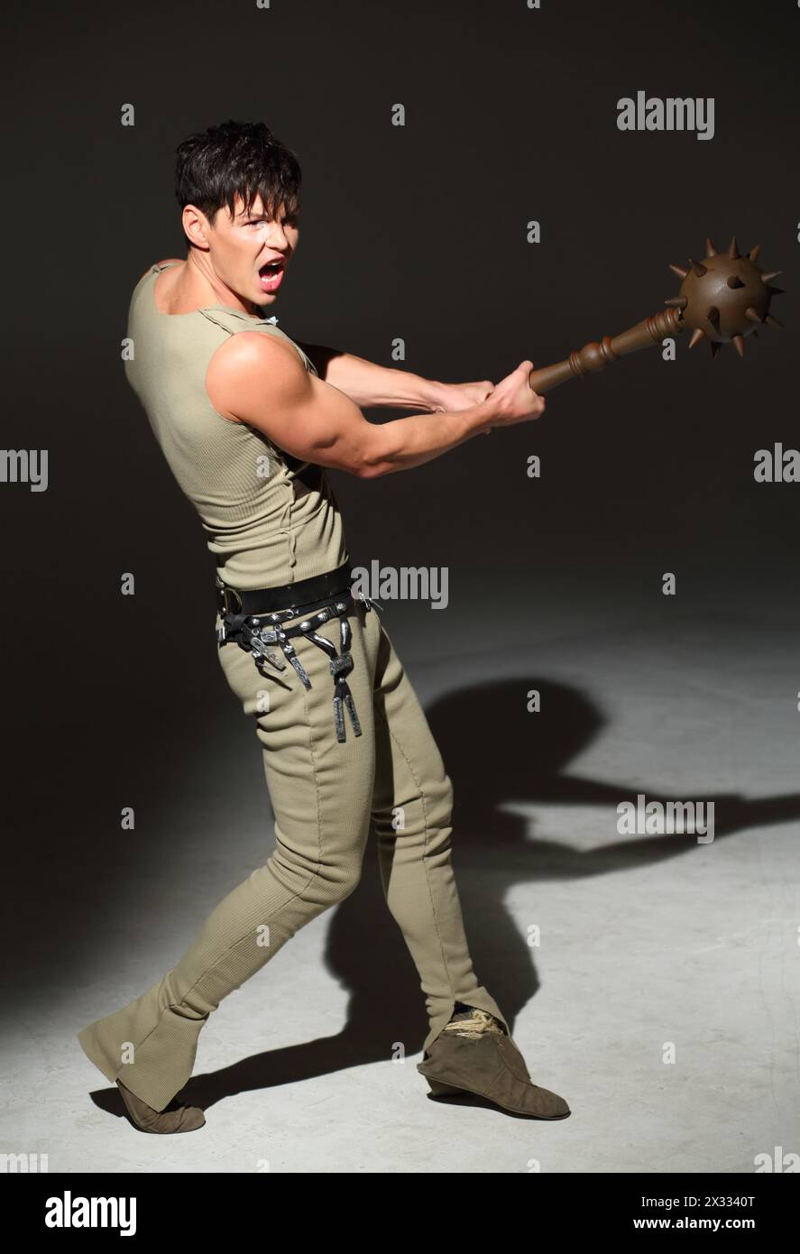 Strong young man in a costume screaming and hit with a mace in a dark ...