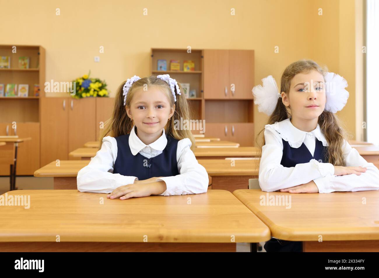 Two happy girls in uniform sit at wooden school desk in classroom at ...