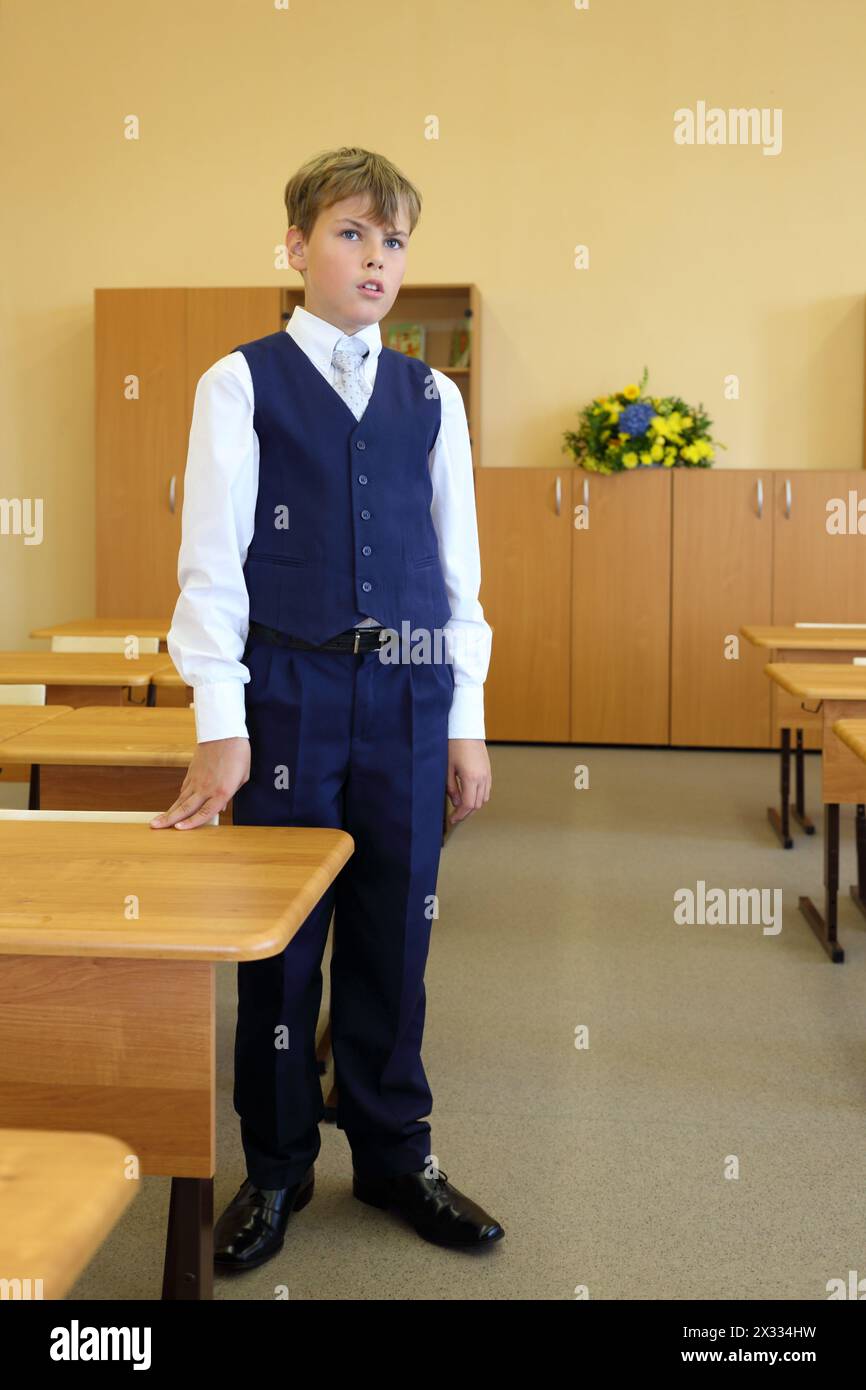 Boy stands next to desk in classroom and answer teacher question in ...