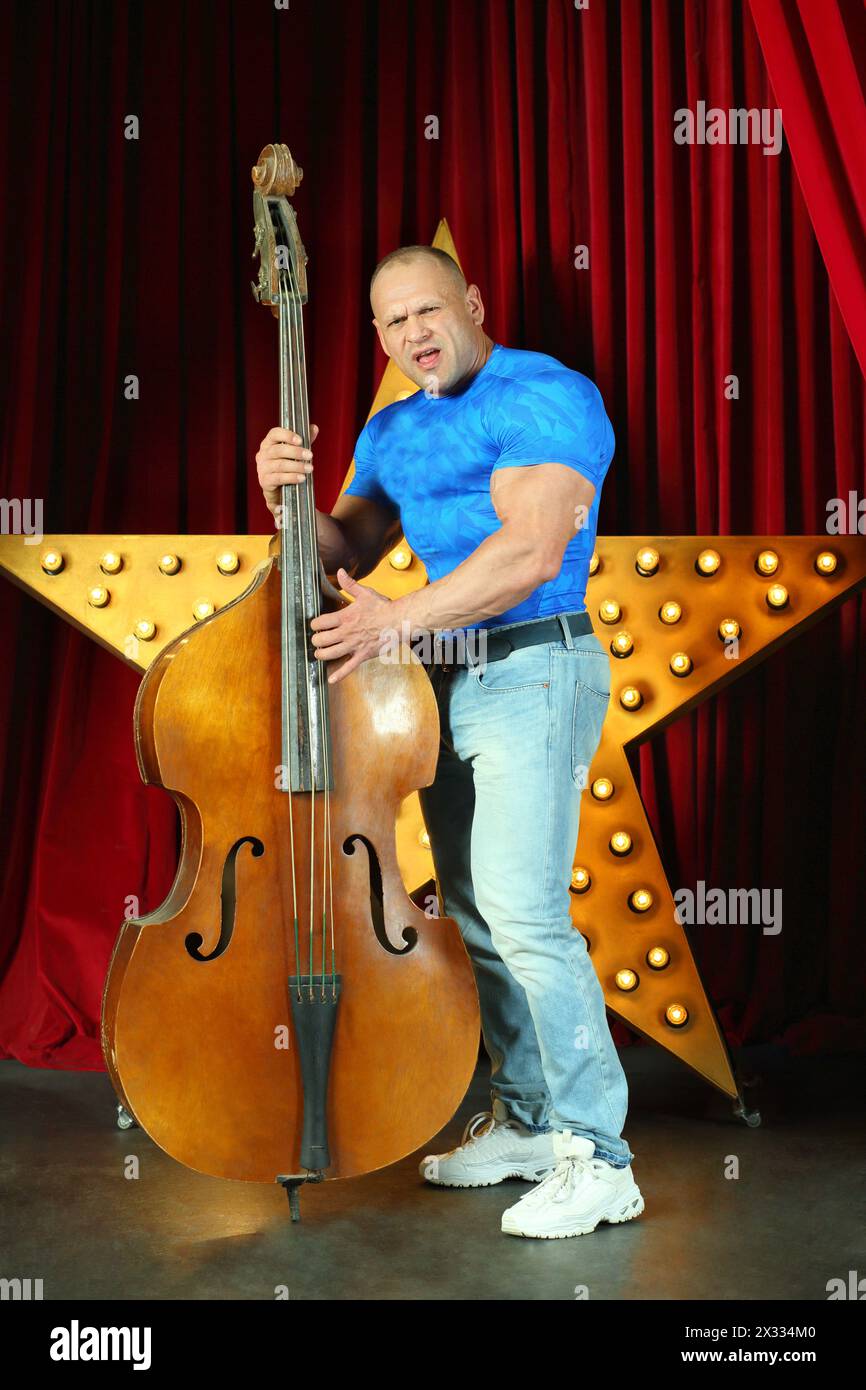 Strong man with big muscles in blue t-shirt playing on stage with ...