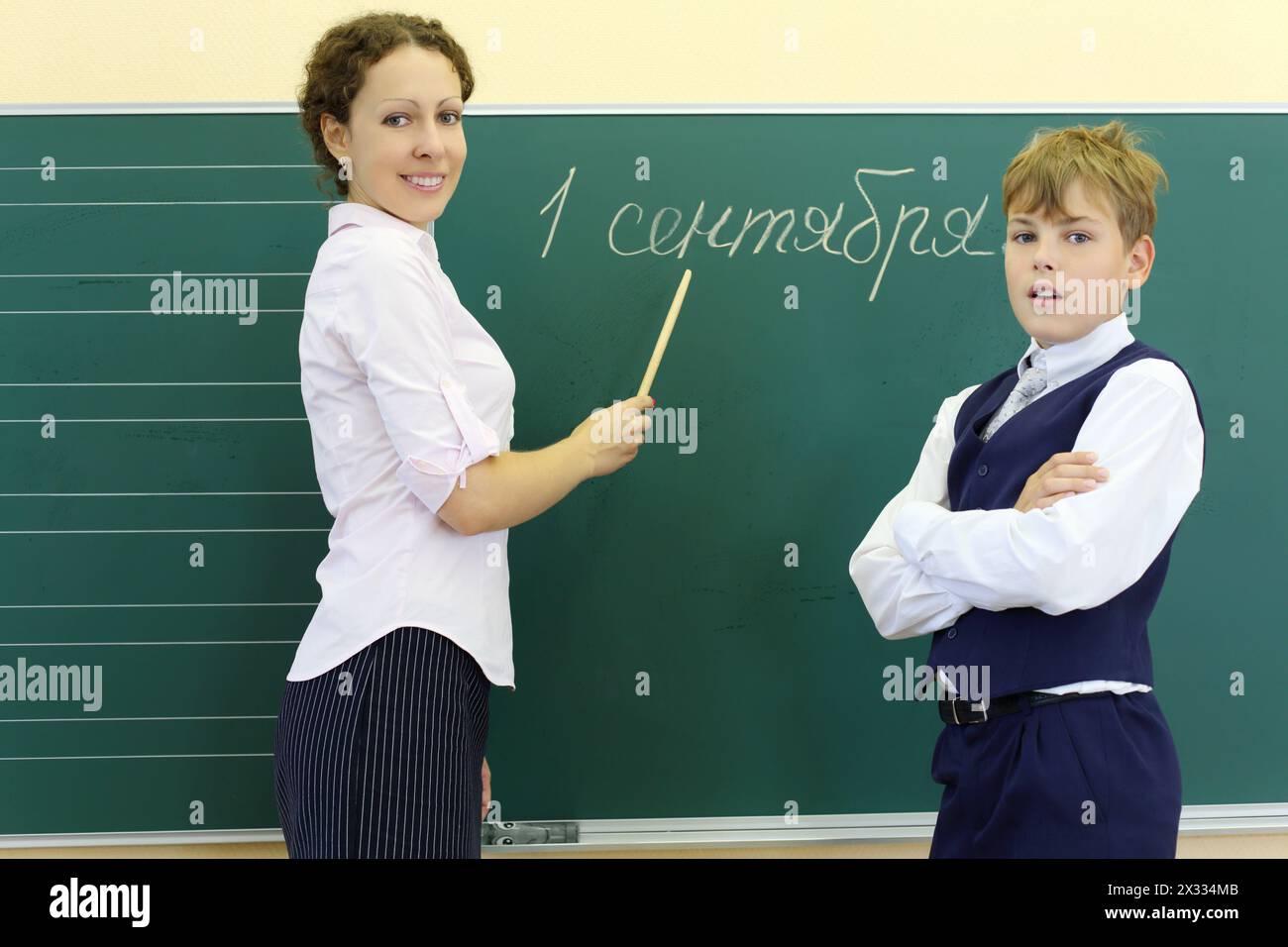 Boy and teacher with pointer stand near chalkboard with inscription ...