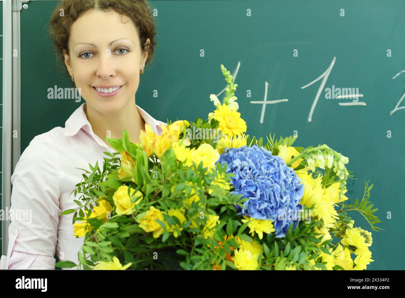 Happy teacher with big bunch of flowers stands near chalkboard in ...