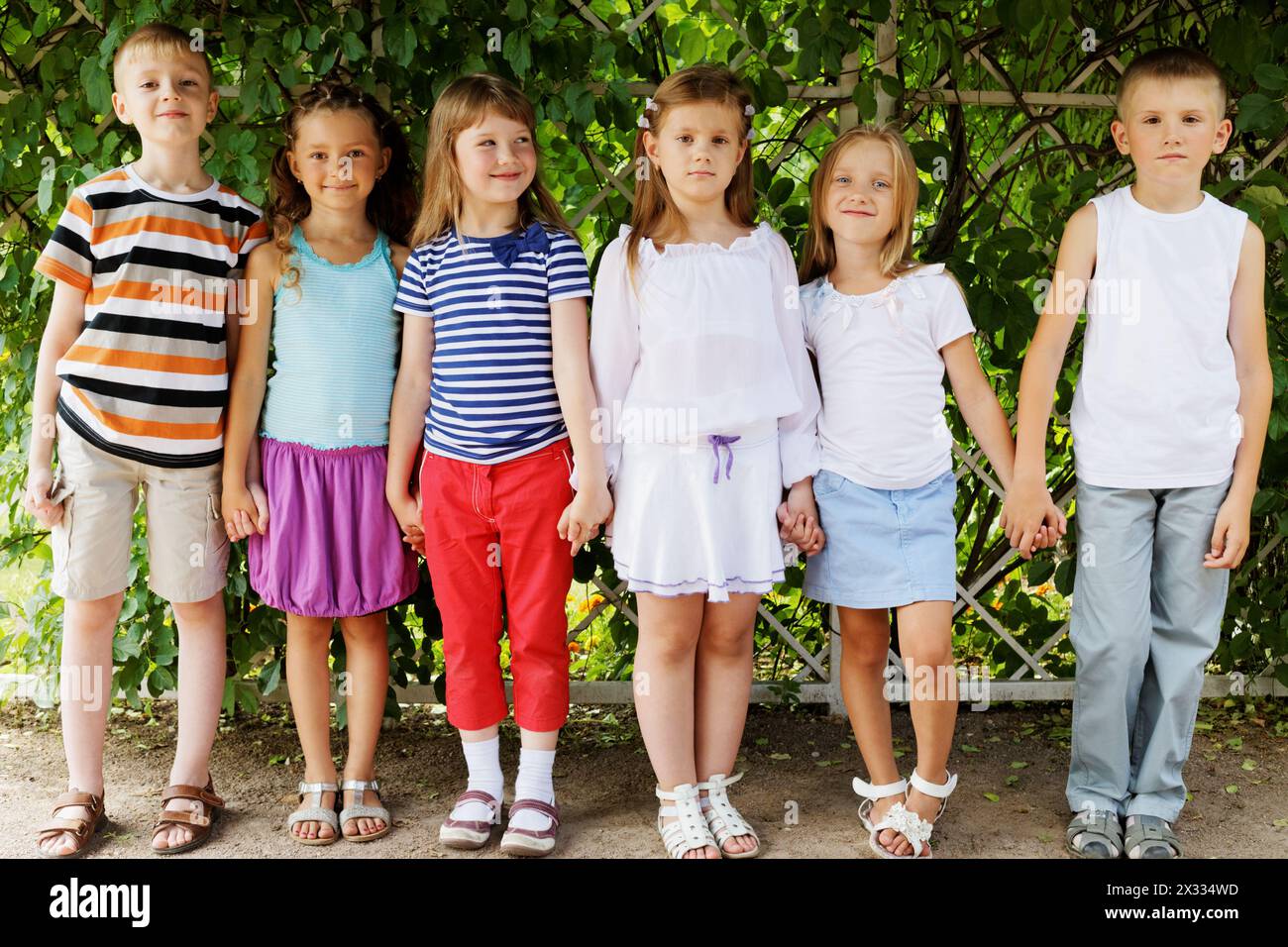 Five children stand holding hands in shadow under arch twined with ...