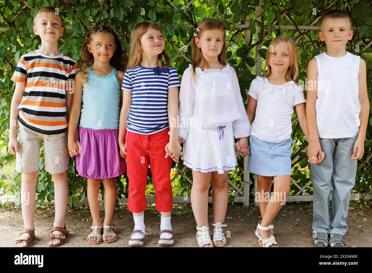 Five children friends stand holding hands in shadow under arch twined ...