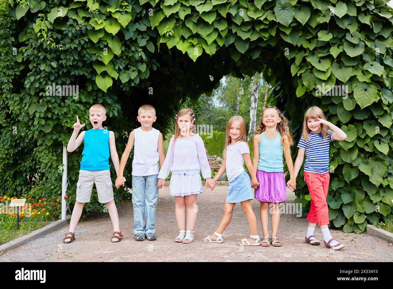 Children stand holding hands with their backs to tunnel made from green ...
