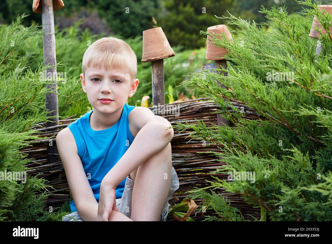 Little boy sits leaning his back on wattle fence Stock Photo - Alamy