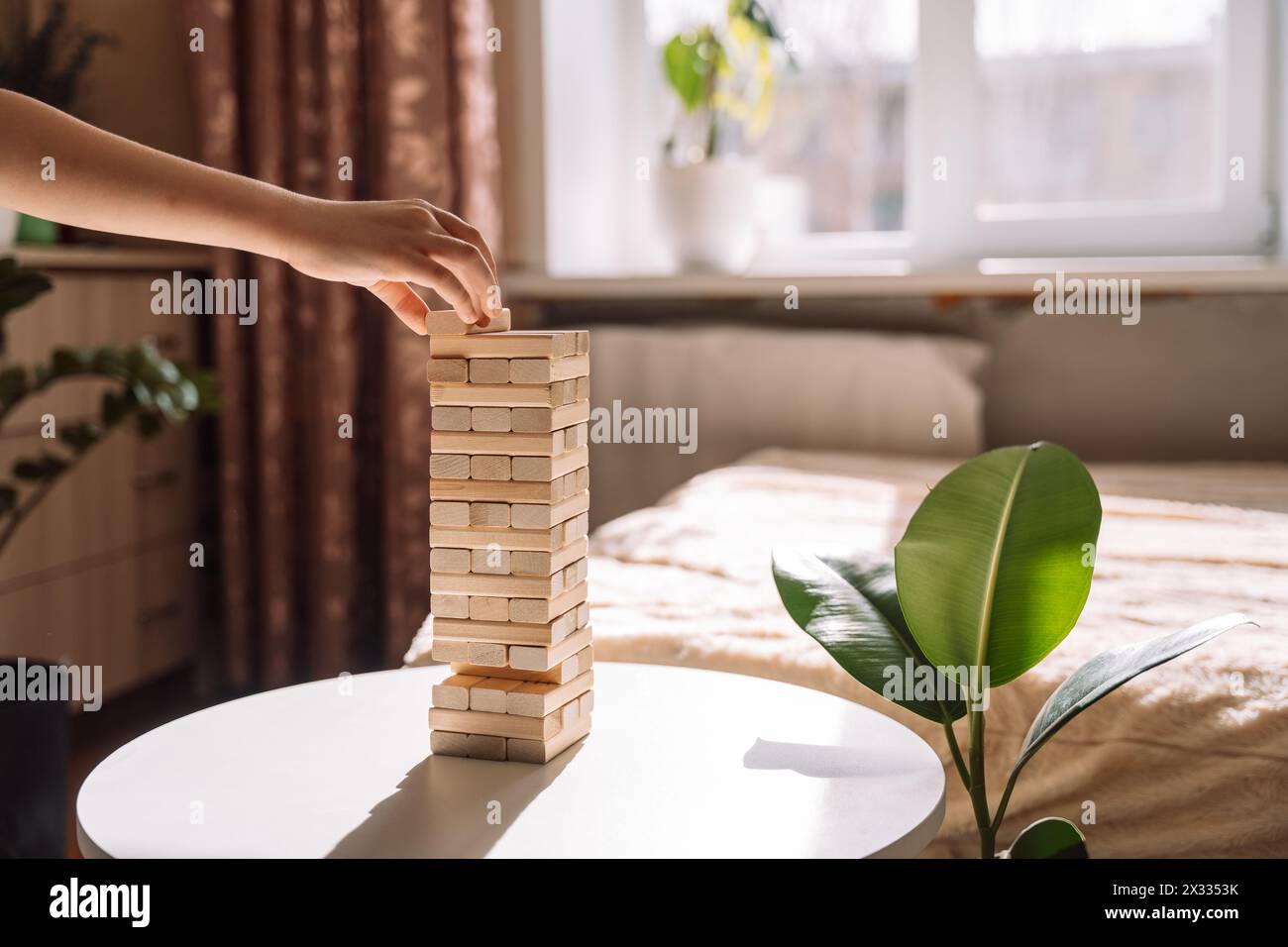 A child slides a wooden block of Jenga game on a white table under ...