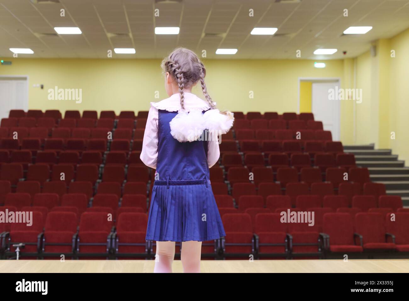 Back of girl with braids and bows standing on stage front of empty ...