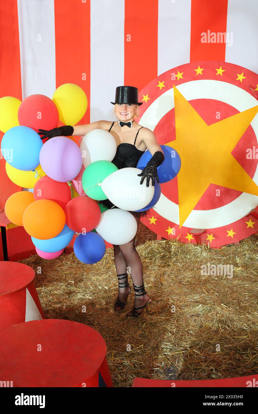 Happy circus actress in black hat with colored balloons in striped ...