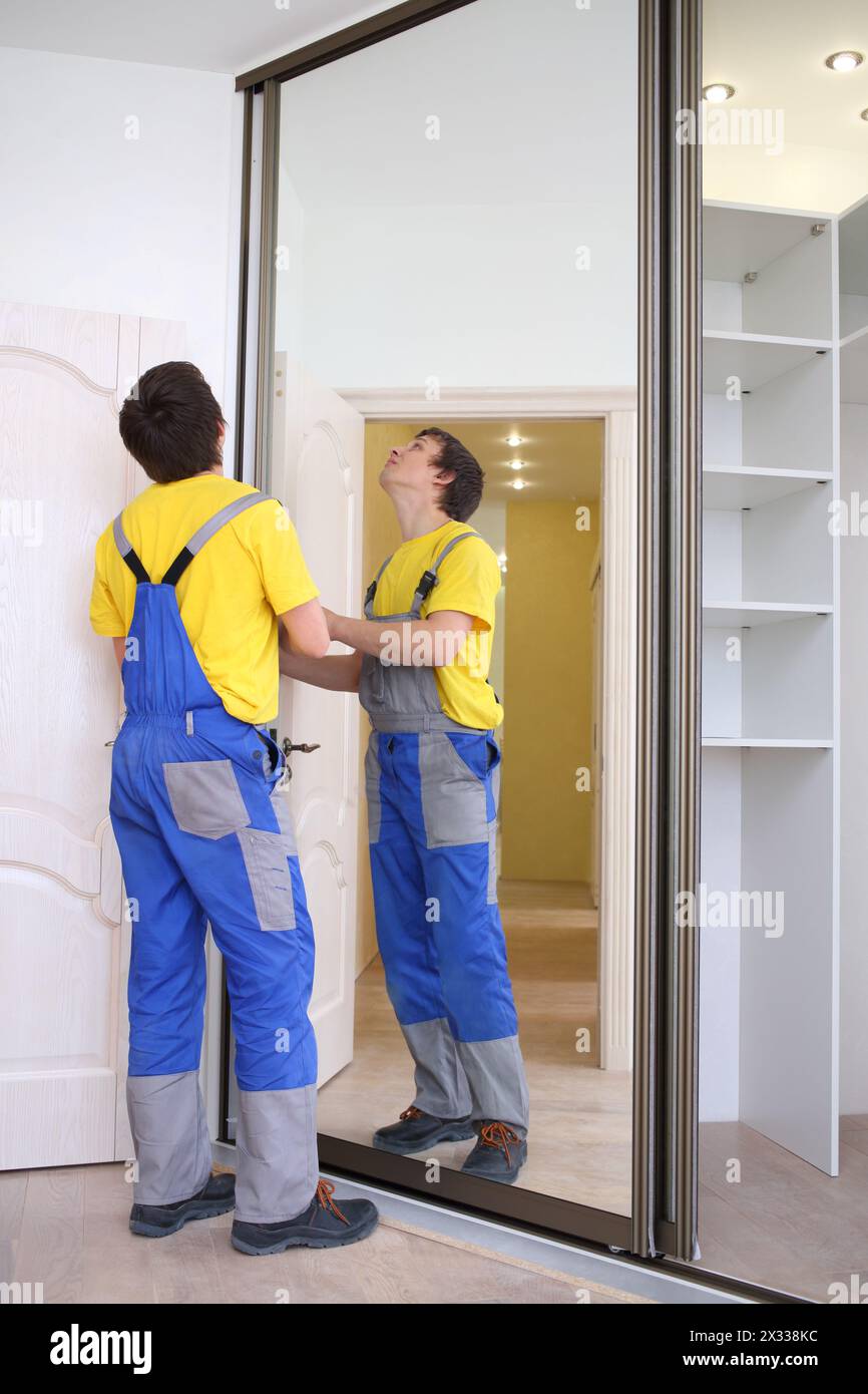 Young man fixing mirrored doors on corner sliding wardrobe in room ...