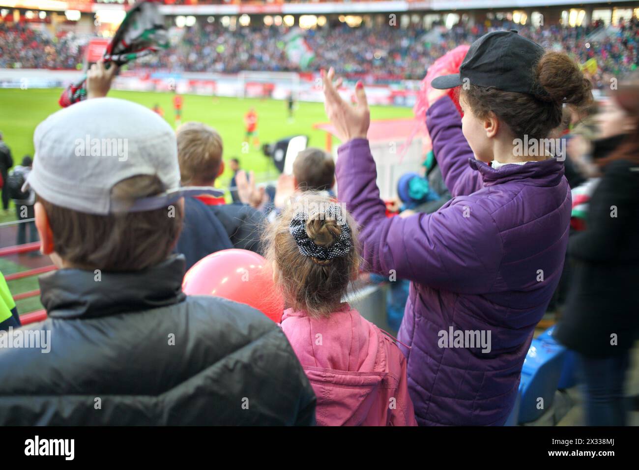 Woman, girl and boy standing applause among fans at a sports stadium ...
