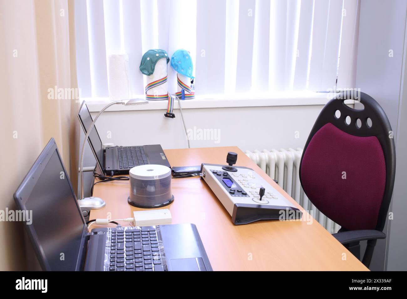 Desk with two laptop computers and remote control near a window with ...