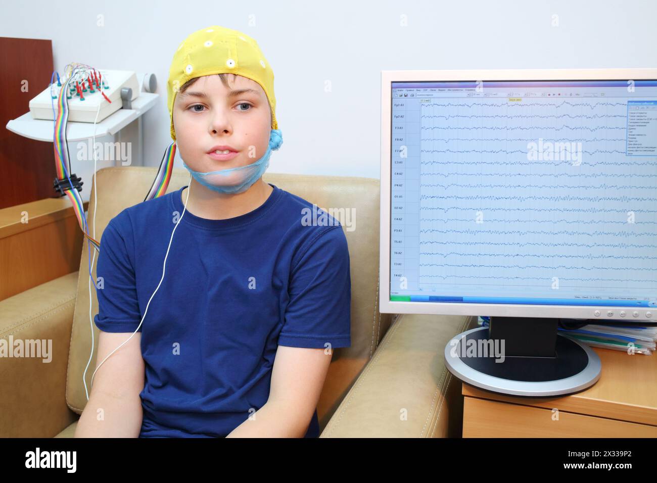 Boy in a special cap during electroencephalography next to the monitor ...