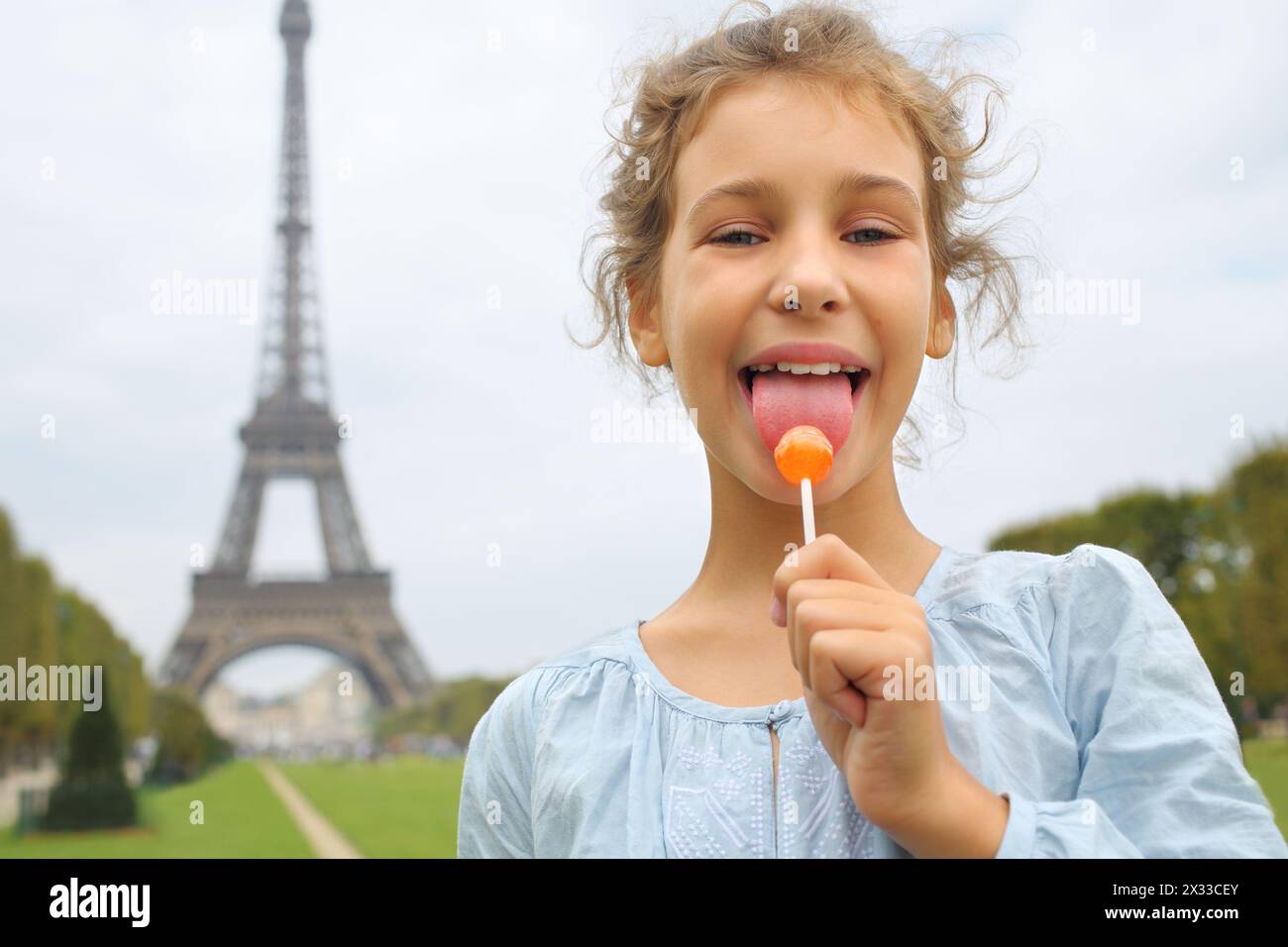 Portrait of a little girl licking a lollipop in front of the Eiffel ...