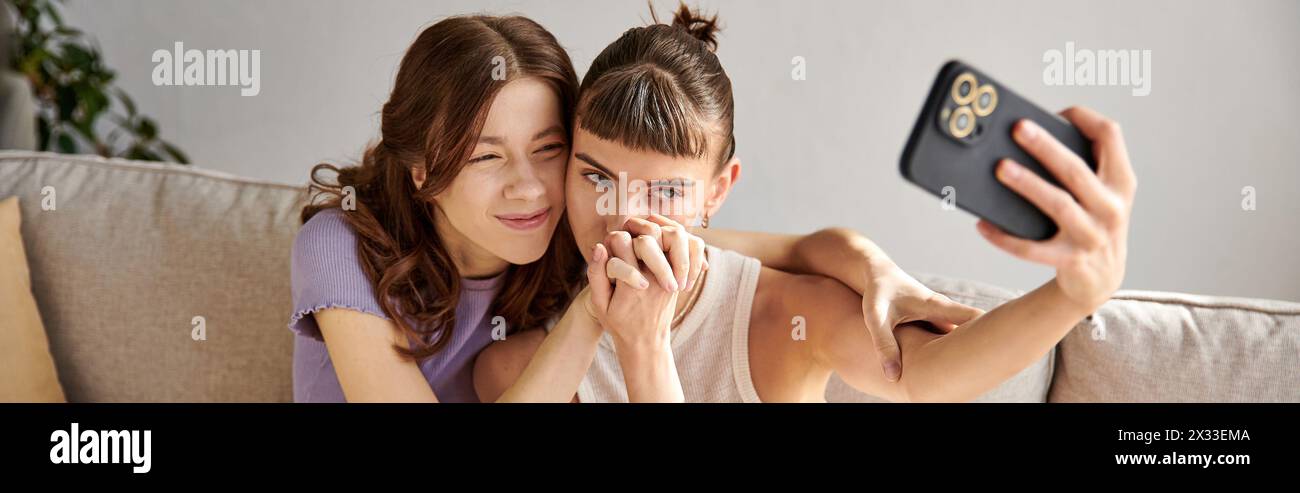 Two women in comfy attire sit on a couch, engrossed in a cell phone ...