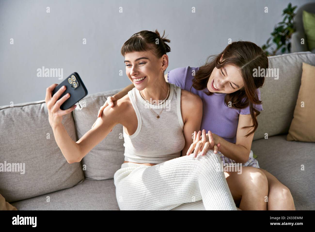 Two women in comfy attire sitting on a couch, engrossed in a cell phone ...