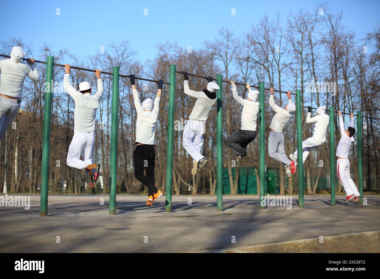 Eight young men training on the horizontal bar on the playground, view ...
