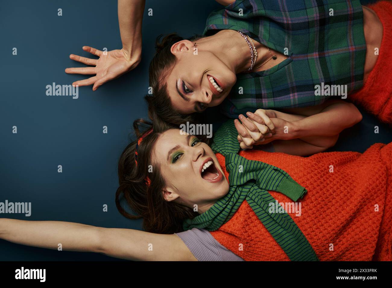 Two women in comfortable attire laying on the ground, arms around each ...